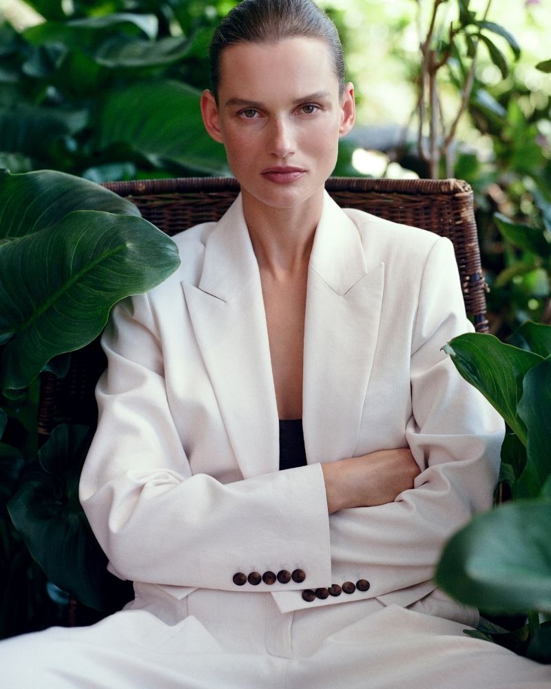 Cream tailored blazer with dark button cuffs layered over a black top%2C styled against lush tropical greenery