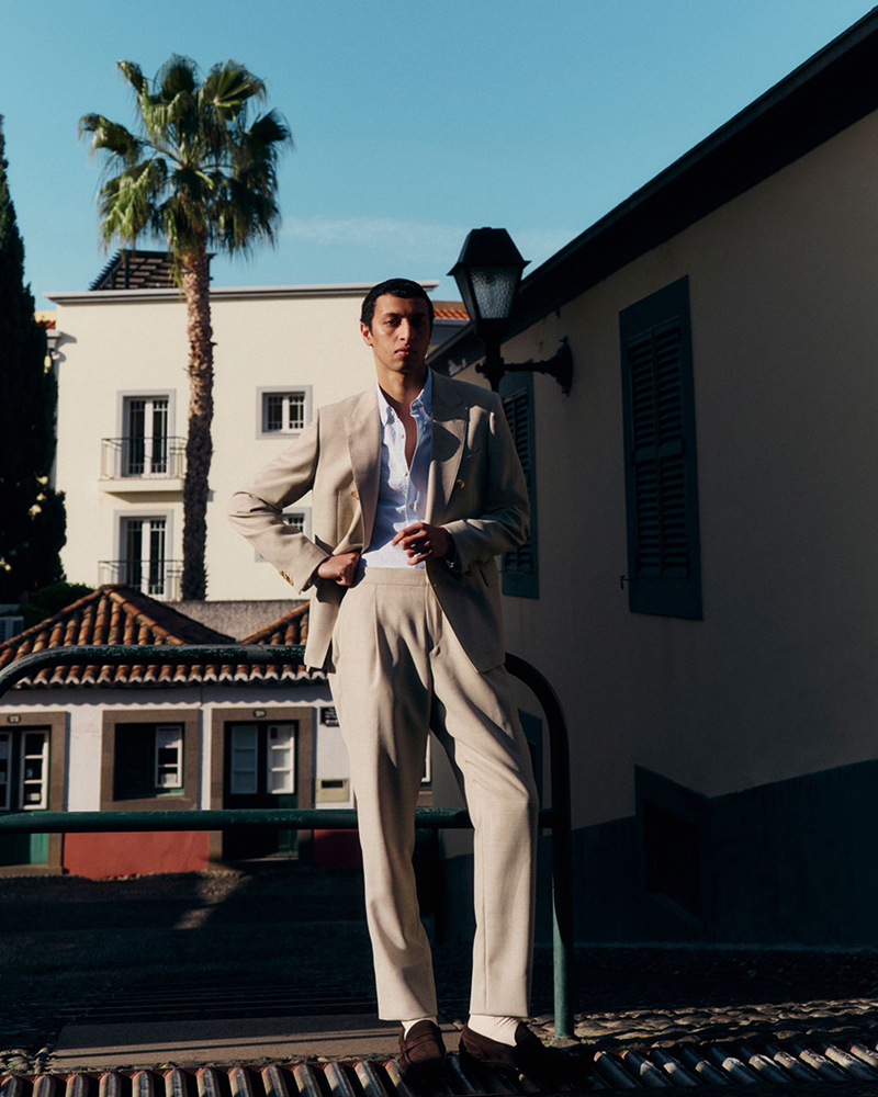 Man in a beige summer suit with loafers and open-collar shirt posed in a Mediterranean courtyard at golden hour