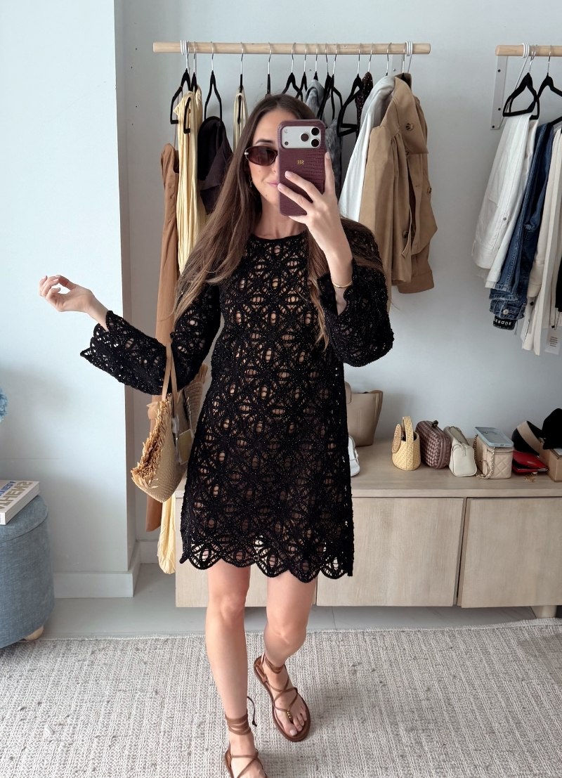 Mirror selfie in a black crochet mini dress with lace-up sandals and woven shoulder bag in a minimalist closet setting