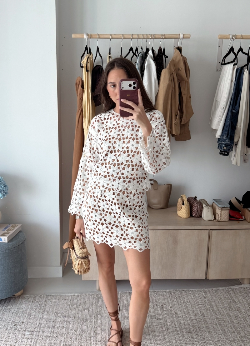 Mirror selfie in a white crochet cover-up dress with lace-up sandals and fringed clutch in a resort-inspired closet setting