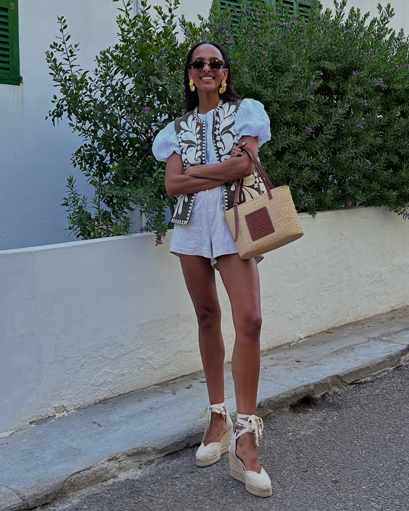White puff-sleeve romper with embroidered vest%2C straw tote and lace-up espadrilles on a Mediterranean street