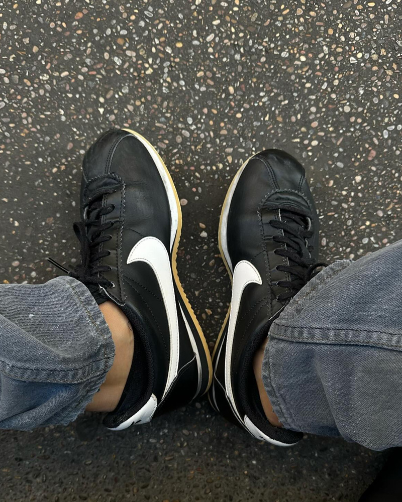 Black and white leather sneakers with gum soles styled with relaxed gray denim on a speckled city sidewalk
