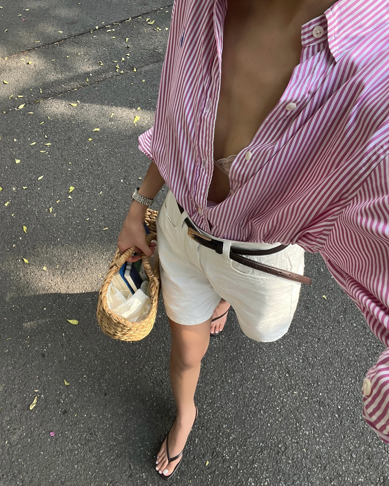 Pink striped button-down shirt styled with white shorts%2C woven basket bag%2C and flip-flops on a sunny city walk