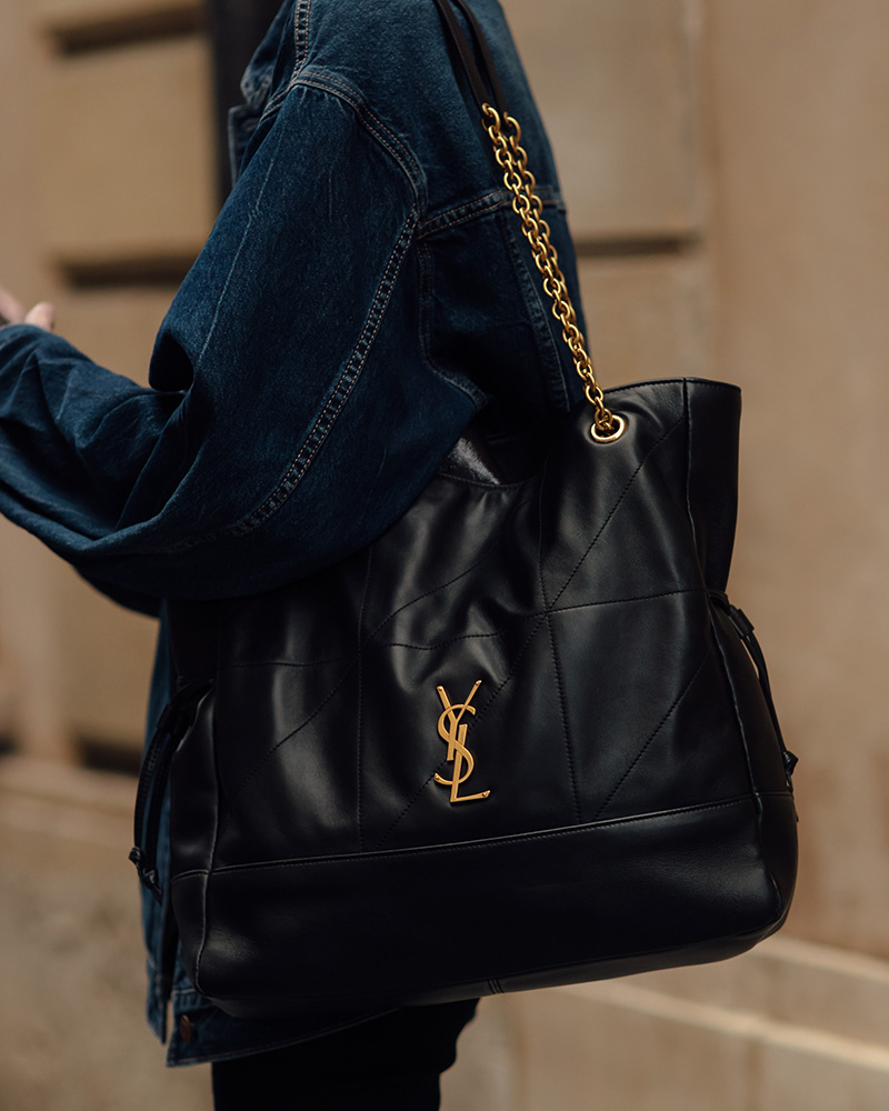 Saint Laurent black quilted leather tote bag with gold YSL logo and chain straps%2C styled with dark denim%0A