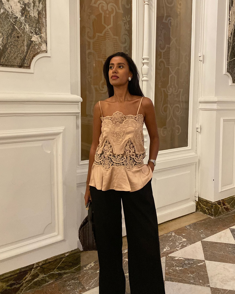 Lace-trim camisole top with wide-leg black trousers and a woven clutch styled in an elegant marble interior