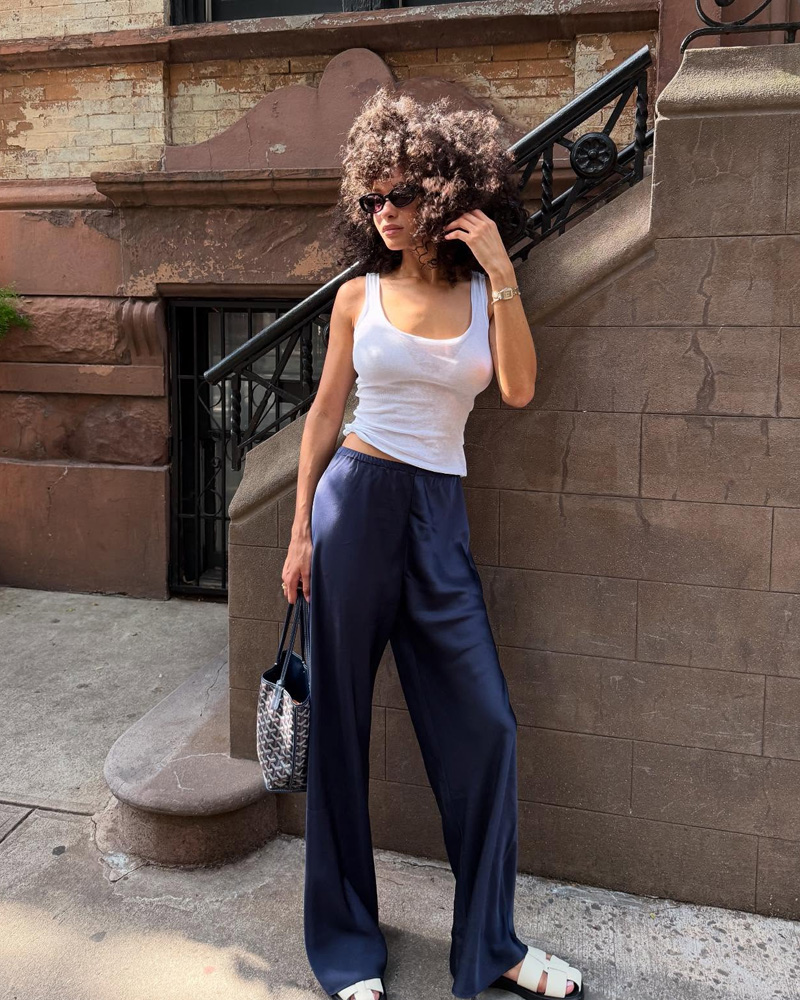 White ribbed tank top with navy satin wide-leg pants%2C woven tote bag and slides styled on a city sidewalk