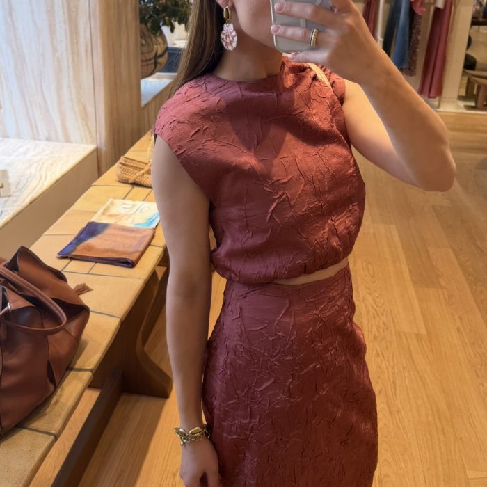 Rust-red crinkled textured crop top and matching midi skirt with statement earrings, styled in a boutique showroom