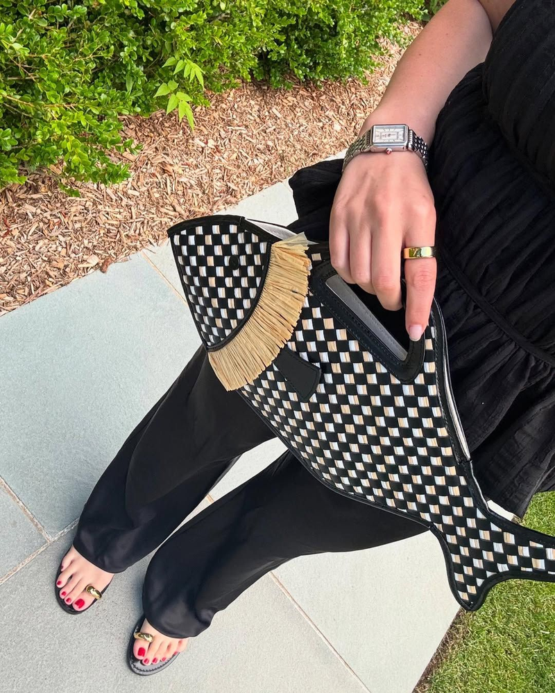 Black and white woven fish-shaped clutch with fringe detail paired with black wide-leg pants%2C gold ring%2C silver watch%2C and black sandals with gold accents.
