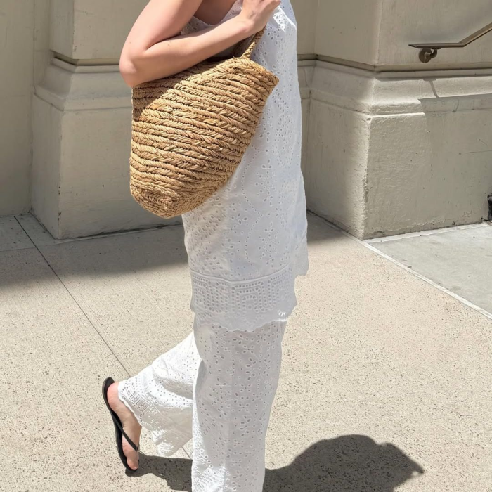 White eyelet cotton sleeveless top and matching pants paired with a woven straw tote bag and black sandals from Balzac Paris.