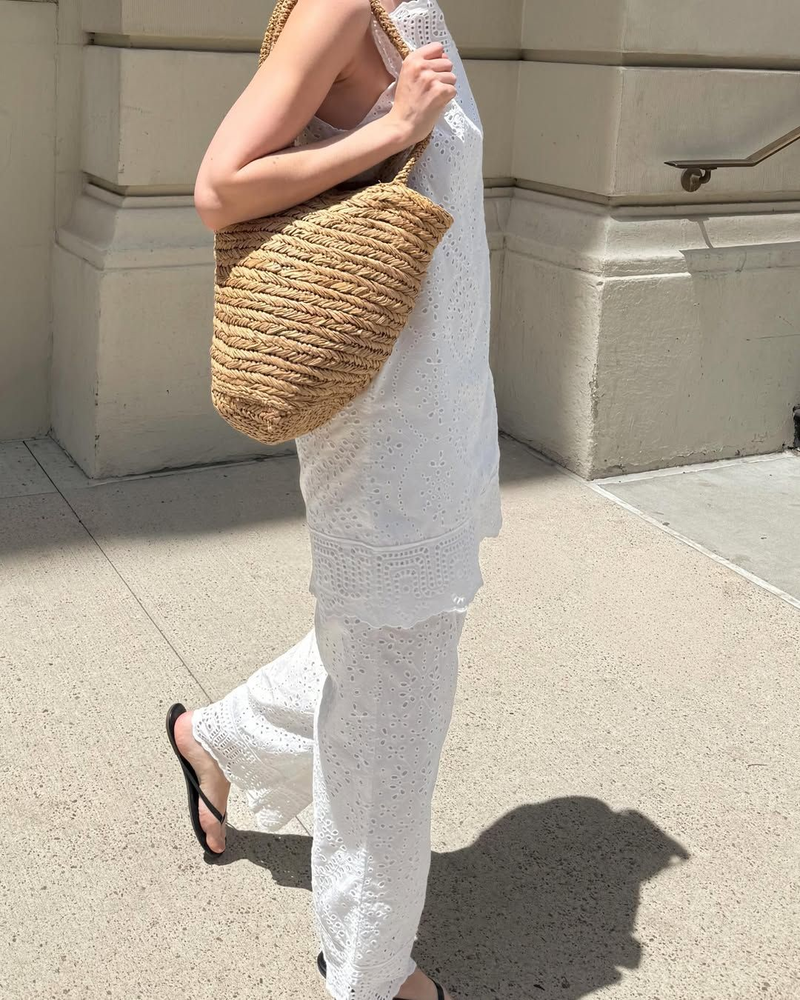 White eyelet cotton sleeveless top and matching pants paired with a woven straw tote bag and black sandals from Balzac Paris