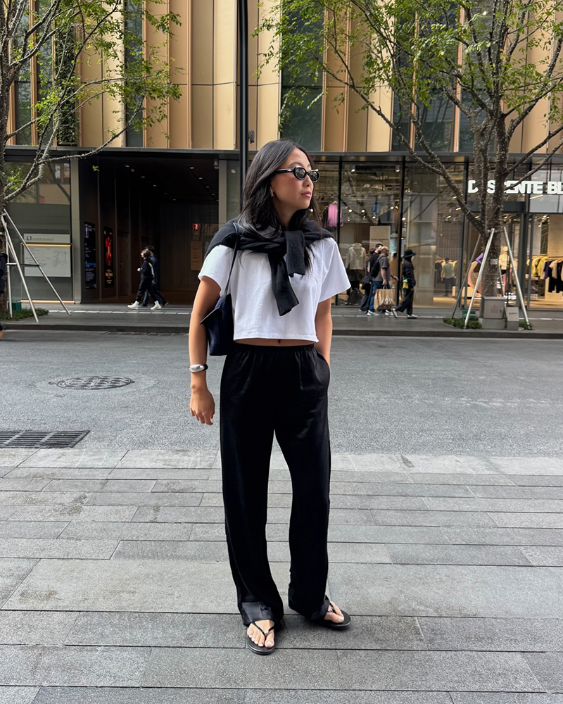 Cropped white T-shirt styled with black wide-leg pants%2C flip-flops and a draped sweater%2C photographed on a modern city street