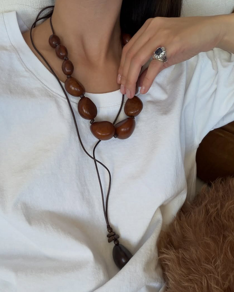 Brown wooden bead pendant necklace styled with a white cotton T-shirt and silver statement ring in a relaxed summer close-up