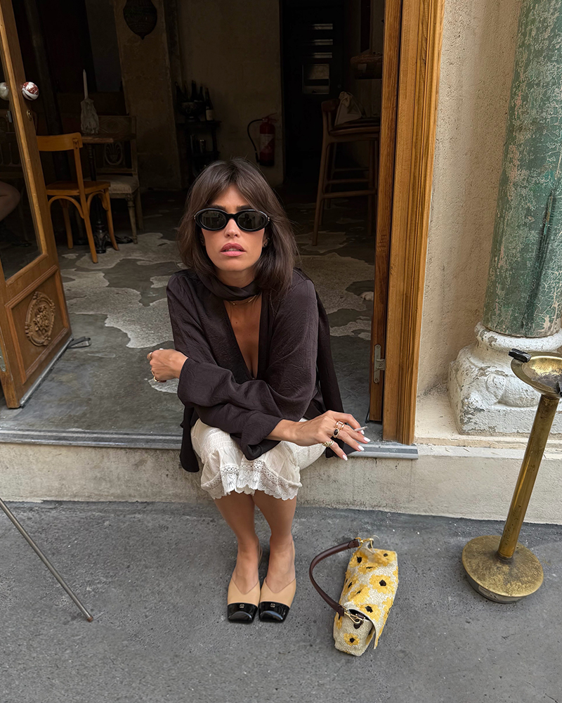 White capri pants paired with a chocolate brown blouse%2C oval sunglasses and a floral woven handbag%2C styled outside a charming caf%C3%A9 entrance