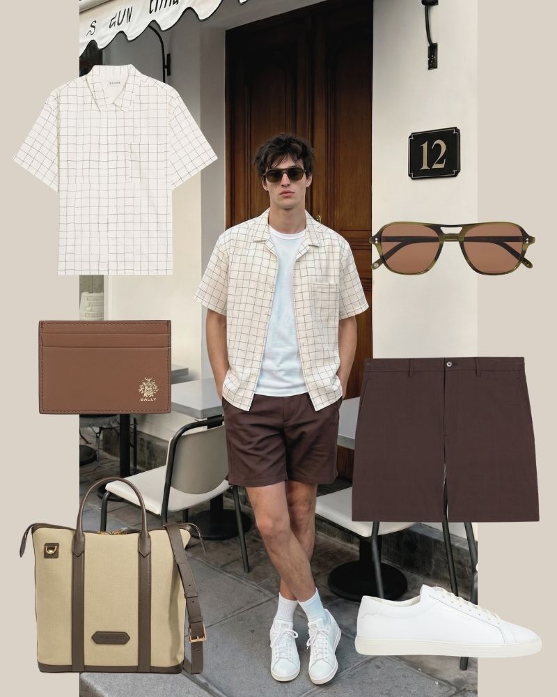 The Outnet men%27s summer outfit with checked camp shirt%2C brown shorts%2C white sneakers and leather accessories outside a caf%C3%A9