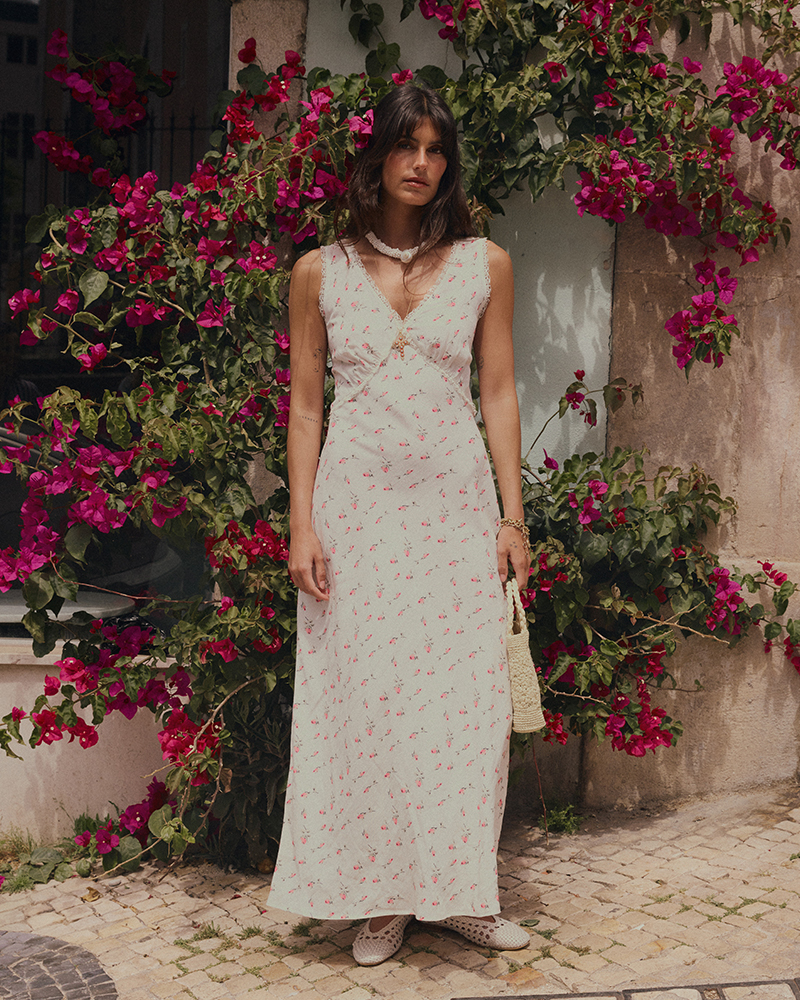 Model in a white floral maxi dress with a woven handbag and mesh flats%2C posed beside vibrant bougainvillea blooms