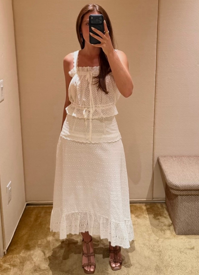 Mirror selfie featuring a white eyelet lace midi dress with tiered ruffles and strappy heels in a fitting room