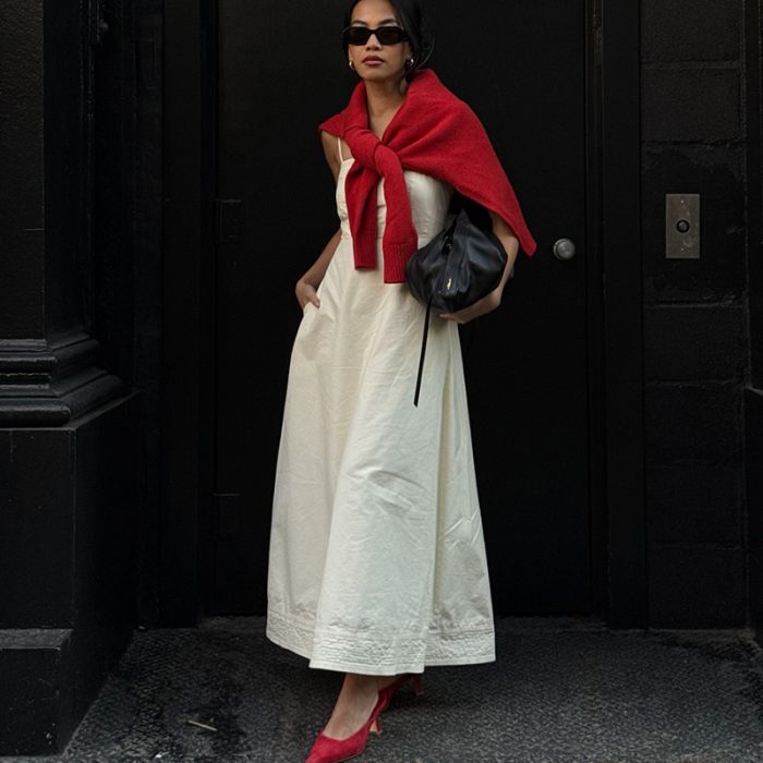 White sleeveless maxi dress styled with a red sweater, black shoulder bag and red pumps against a dark city doorway