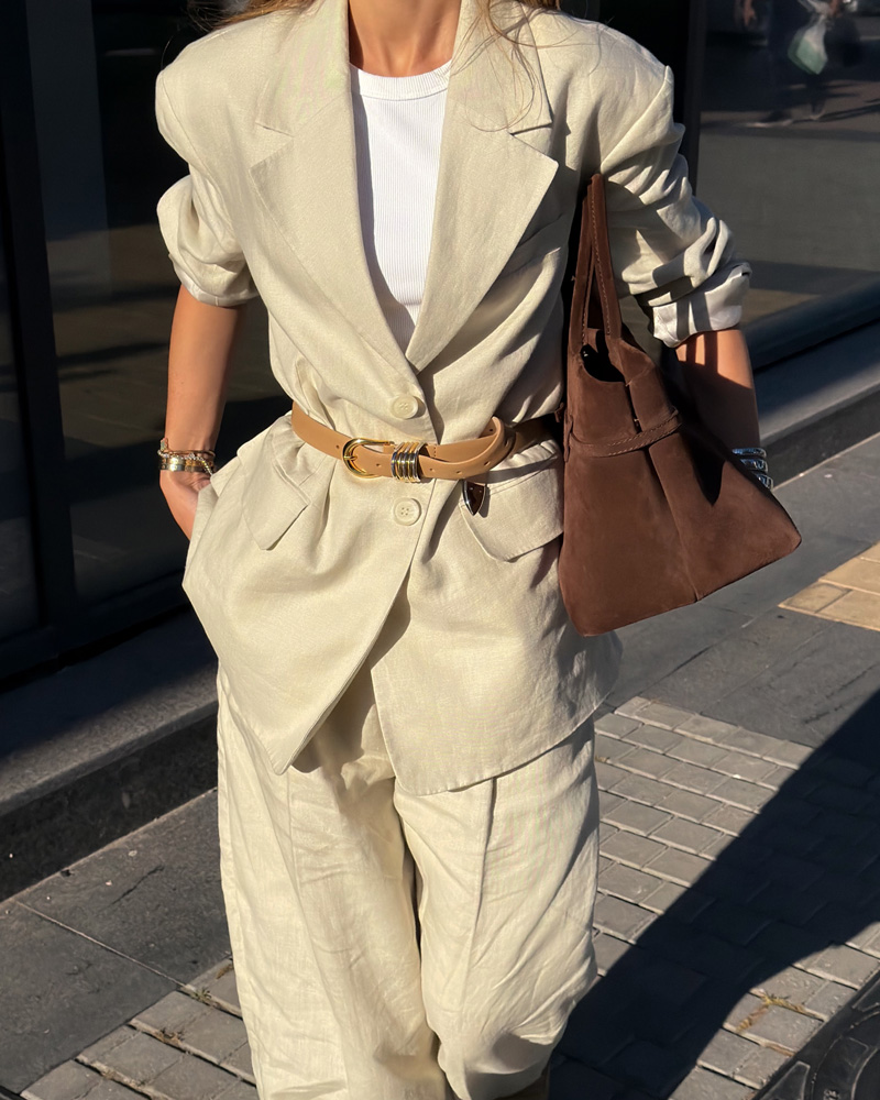 Woman in a cream linen blazer and wide-leg trousers%2C styled with a tan belt and brown suede tote on a city street
