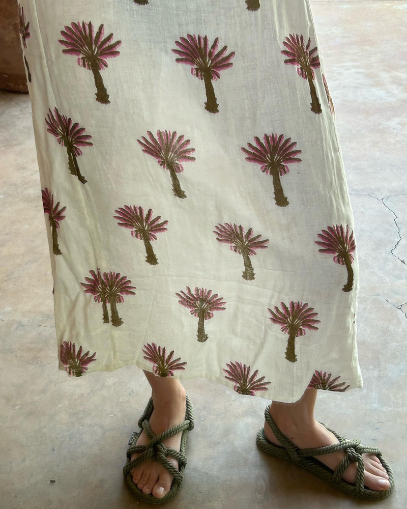 Close-up of olive rope sandals paired with a white palm print maxi dress%2C styled on a polished concrete floor