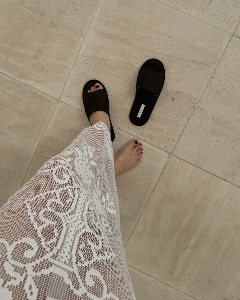 White lace crochet cover-up paired with black slide sandals%2C styled on a neutral stone floor for a chic summer resort look