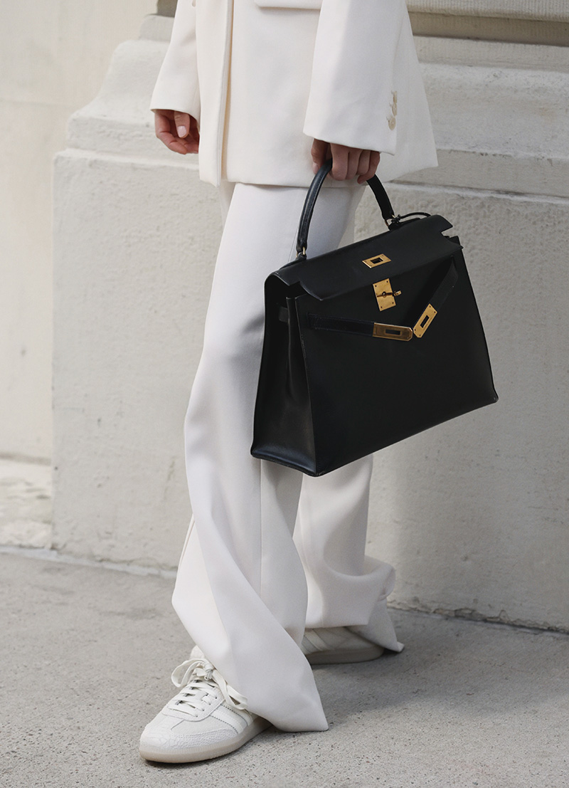 White oversized pantsuit with black leather tote, slim sunglasses and white sneakers on a minimalist city street backdrop