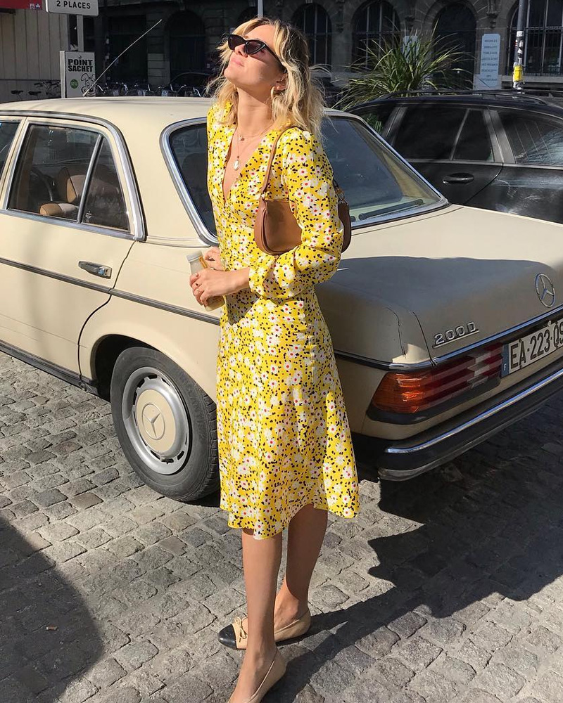 Yellow floral wrap midi dress styled with cat-eye sunglasses%2C a brown shoulder bag and flats beside a vintage car on a sunlit street