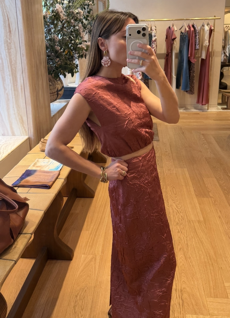 Rust-red crinkled crop top and matching midi skirt with statement earrings, styled in a boutique showroom