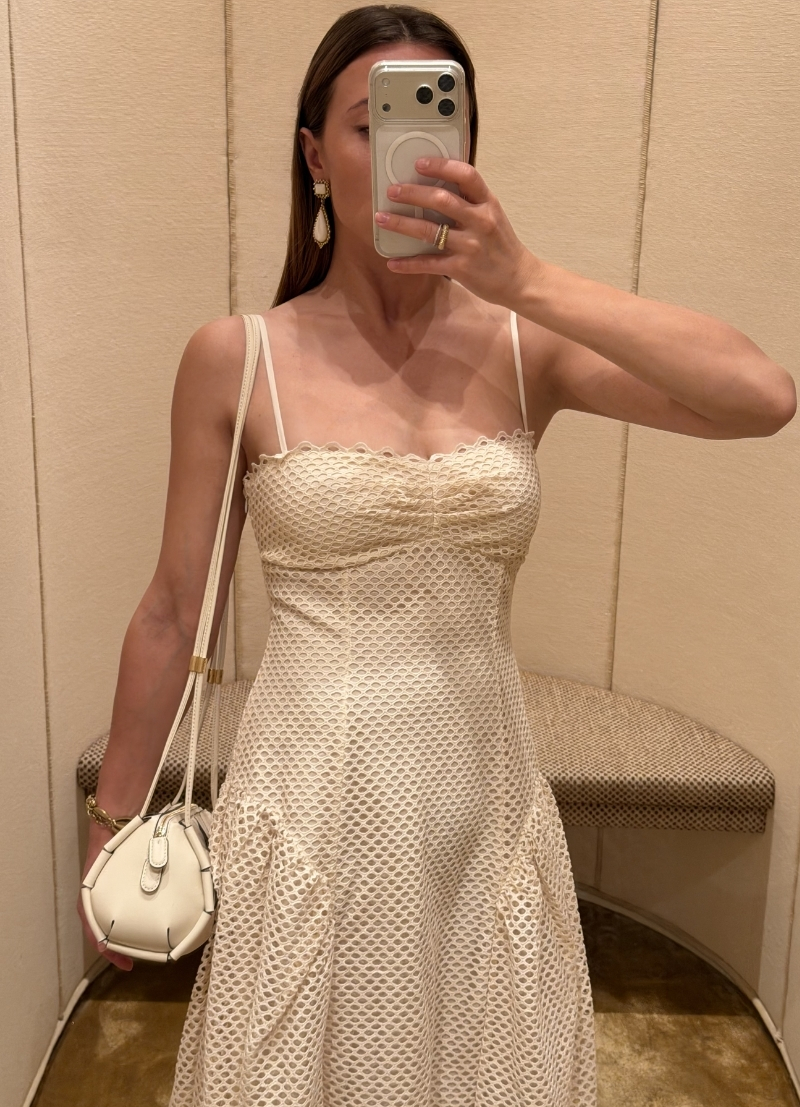 Cream mesh midi dress with delicate straps and a white woven mini bag, styled in a boutique fitting room