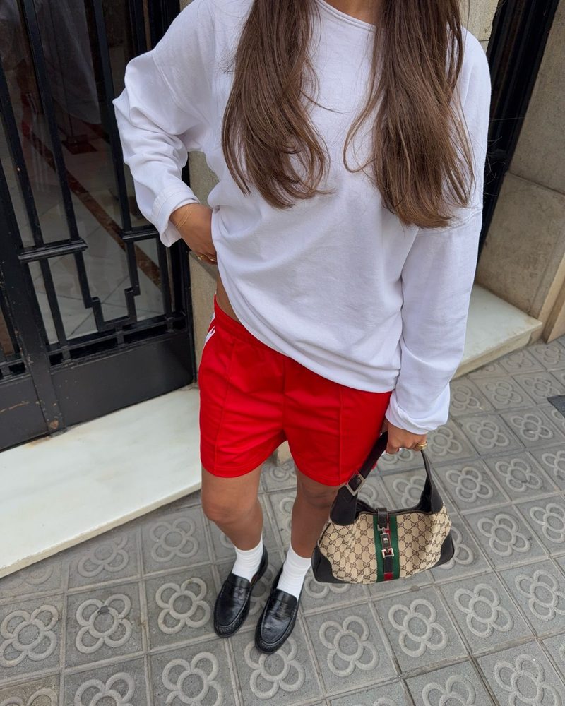 Sporty casual outfit featuring a relaxed white oversized sweatshirt%2C red athletic shorts%2C and a chic Gucci hobo bag with a signature canvas print.