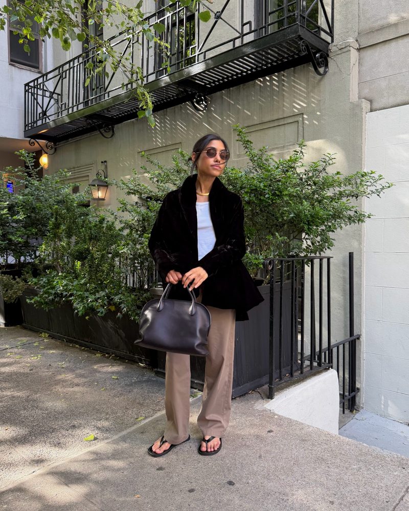 Chic fall outfit featuring a velvet black blazer over a gray top%2C paired with beige wide-leg trousers and sleek black flip-flops.