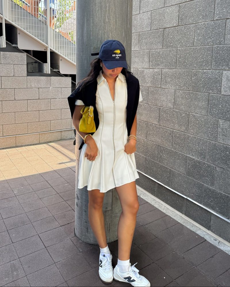 Chic summer outfit featuring a zip-up white dress%2C paired with New Balance sneakers and a stylish navy cap for a sporty vibe