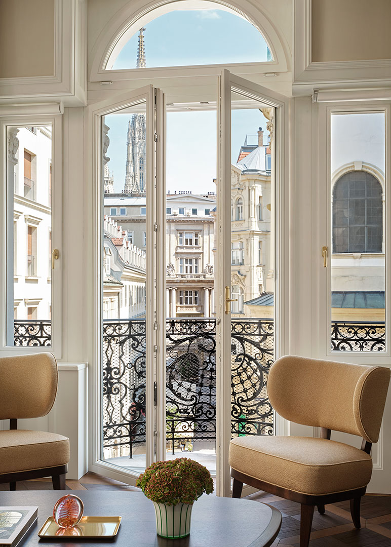 Luxury hotel suite with French doors opening to a historic city view, styled with modern armchairs and elegant décor