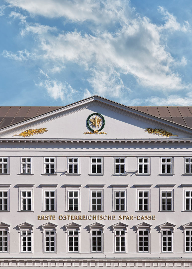 Historic white neoclassical building with gilded architectural details beneath a bright blue sky in Vienna