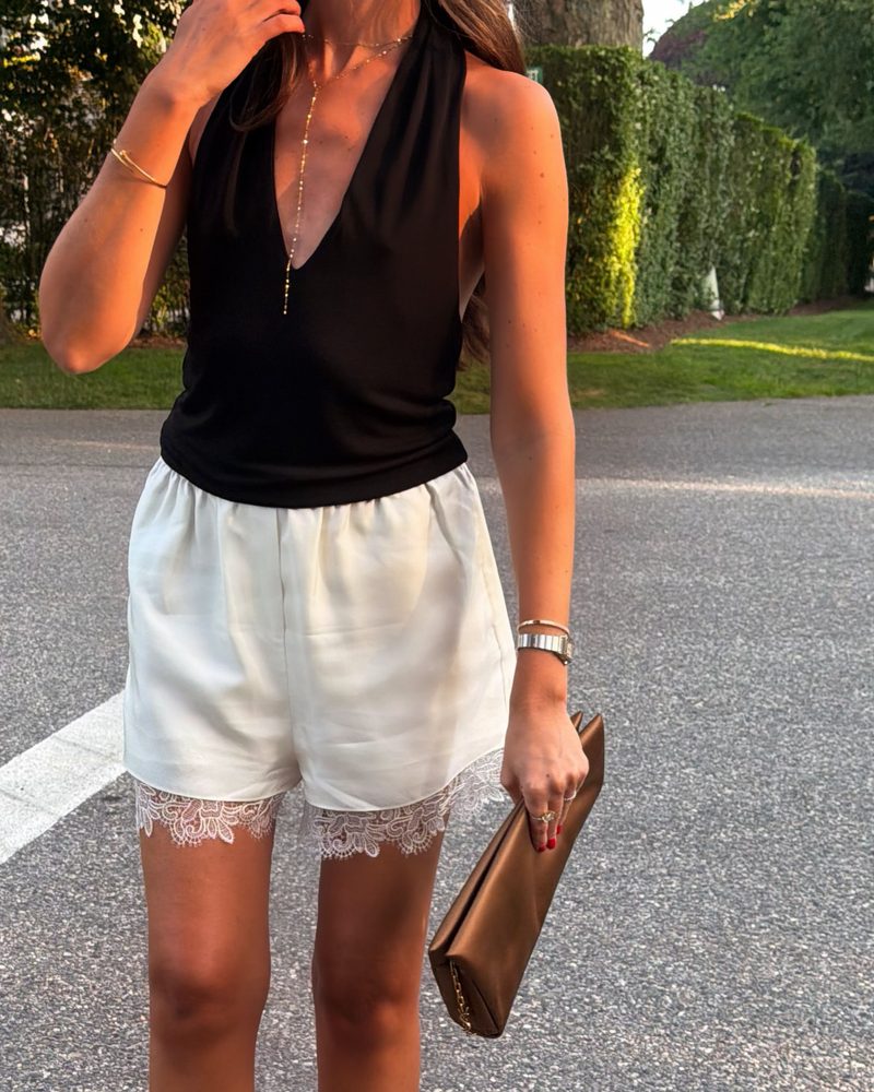 Sleek black halter top paired with light cream shorts featuring intricate lace trim%2C accessorized with a chic gold clutch and layered jewelry