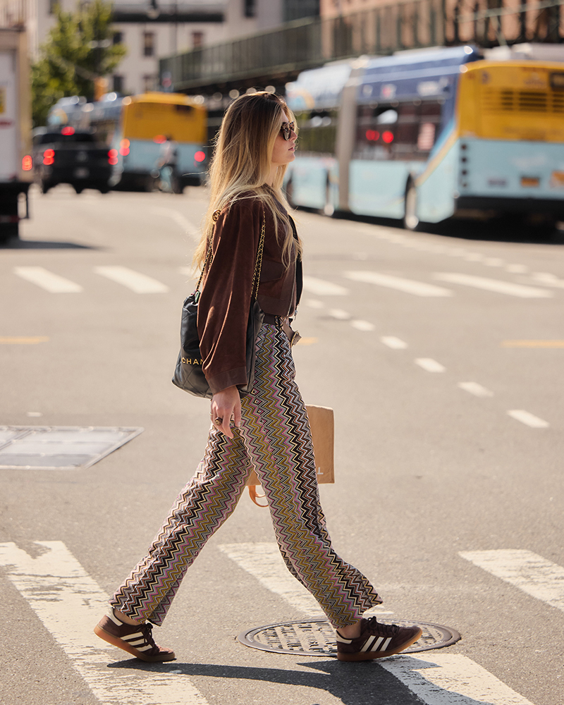 Brown Adidas sneakers paired with zigzag trousers%2C cropped jacket and Chanel bucket bag%2C styled on a city crosswalk