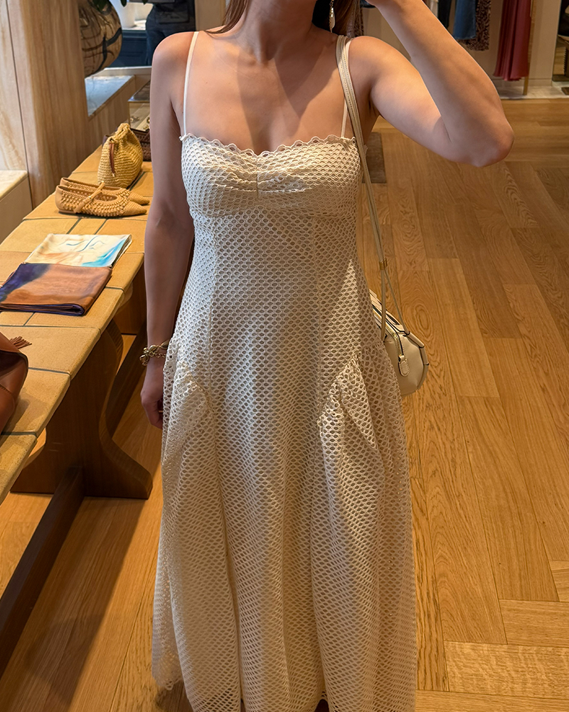 White textured spaghetti-strap midi dress paired with a cream shoulder bag%2C photographed in a luxury boutique fitting room