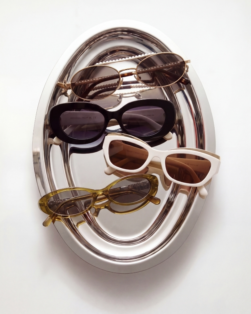 Chanel sunglasses collection featuring oval and cat-eye frames in black%2C white and tortoiseshell on a mirrored tray