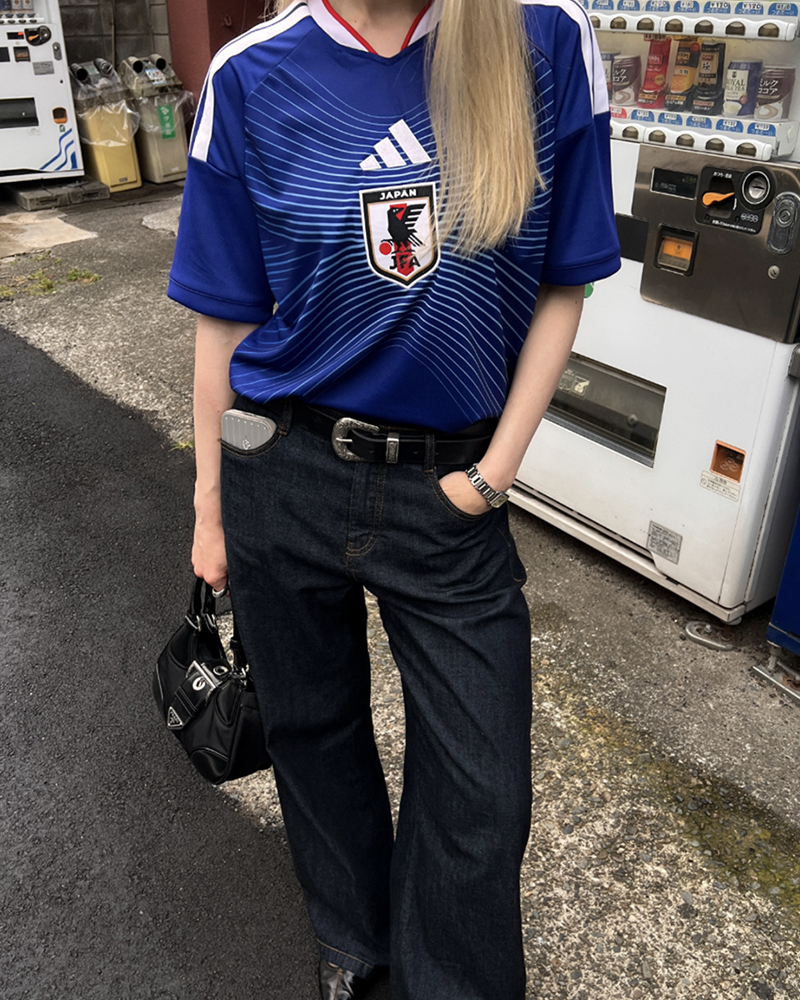 Adidas Japan national team soccer jersey styled with dark wide-leg jeans%2C black handbag and Western belt on an urban street