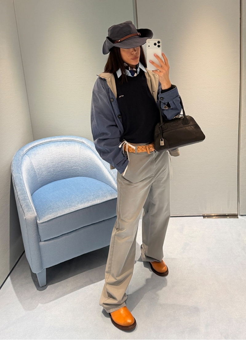 Miu Miu mirror selfie featuring a navy layered jacket, wide-leg trousers, leather handbag and bucket hat in a minimalist fitting room
