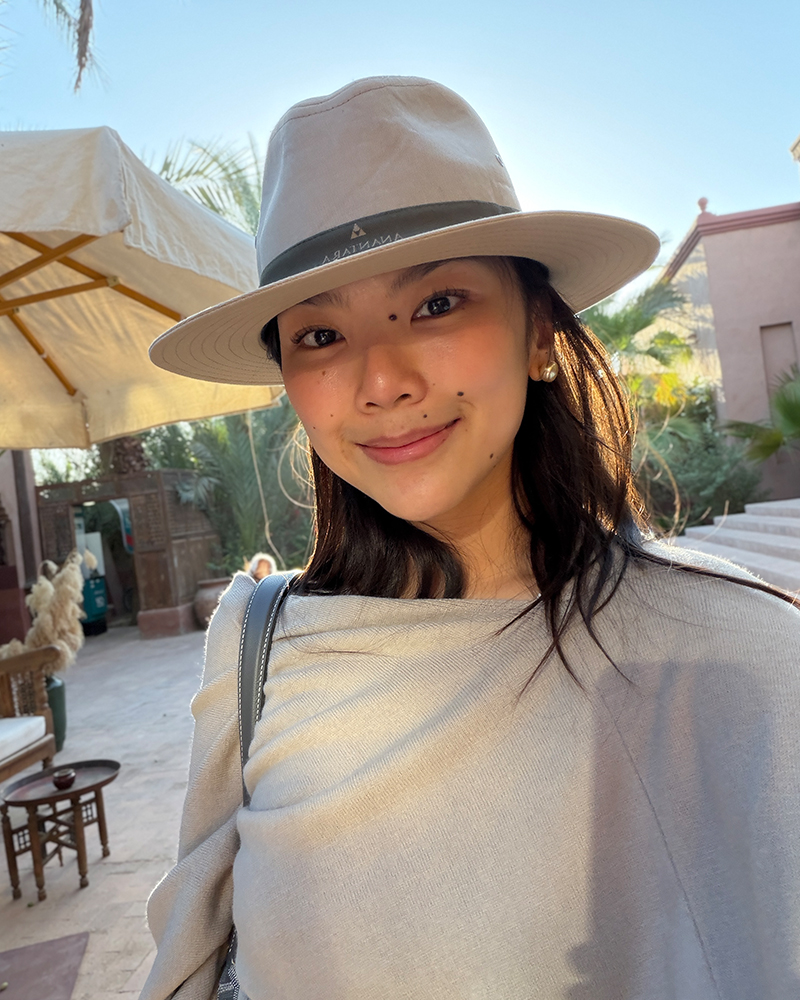 Wide-brim sun hat paired with a light gray draped knit top and shoulder bag%2C captured in a sunlit resort courtyard