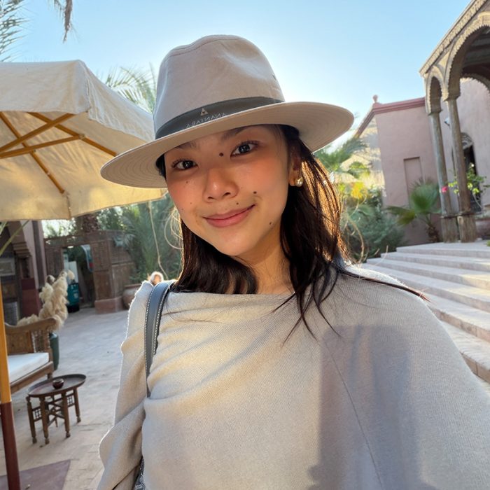 Wide-brim sun hat paired with a light gray draped knit top and shoulder bag, captured in a sunlit resort courtyard