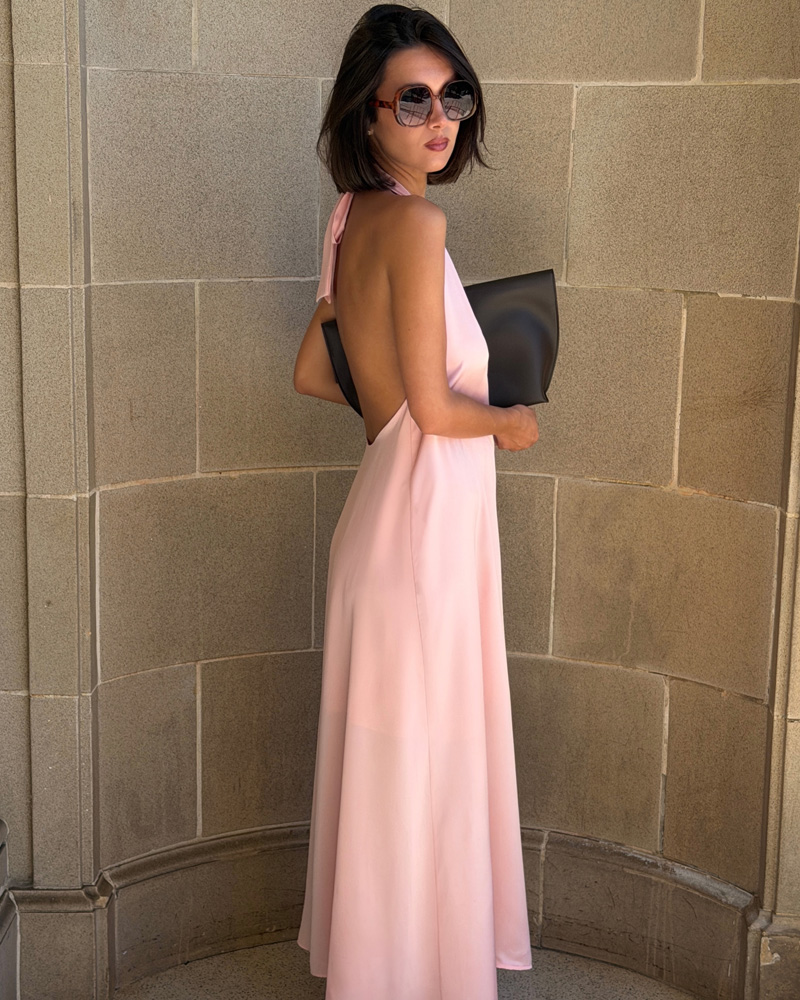 Blush pink halter maxi dress styled with oversized sunglasses and a black clutch against a stone architectural backdrop%0A