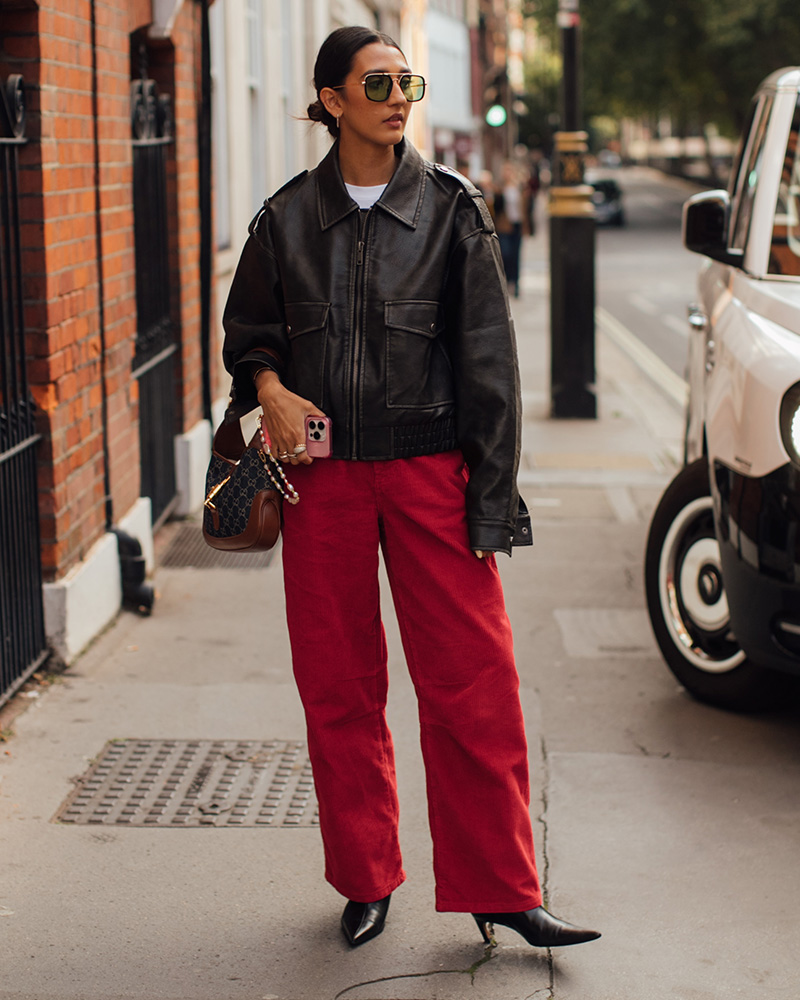 Street style featuring a black leather bomber jacket%2C red wide-leg pants and pointed ankle boots on a city sidewalk%0A