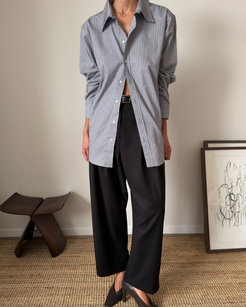 Oversized gray striped button-down shirt with black wide-leg trousers and pointed heels%2C styled in a minimalist interior