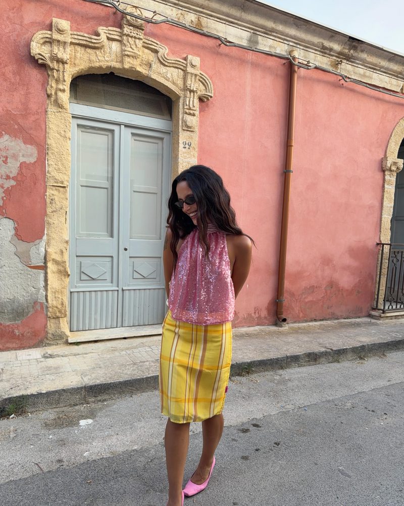 Woman wearing a pink sequin halter top paired with a yellow plaid pencil skirt and pink pointed-toe heels in a street setting.
