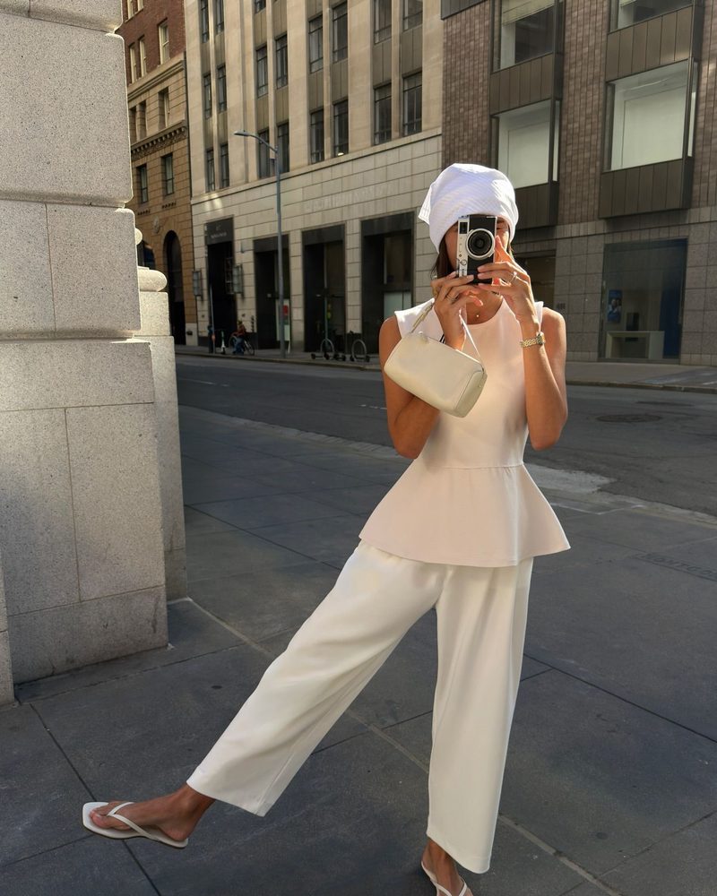 A person in stylish white clothing and sandals%2C with a white head wrap%2C takes a photo on a city street%2C conveying a chic and urban vibe.