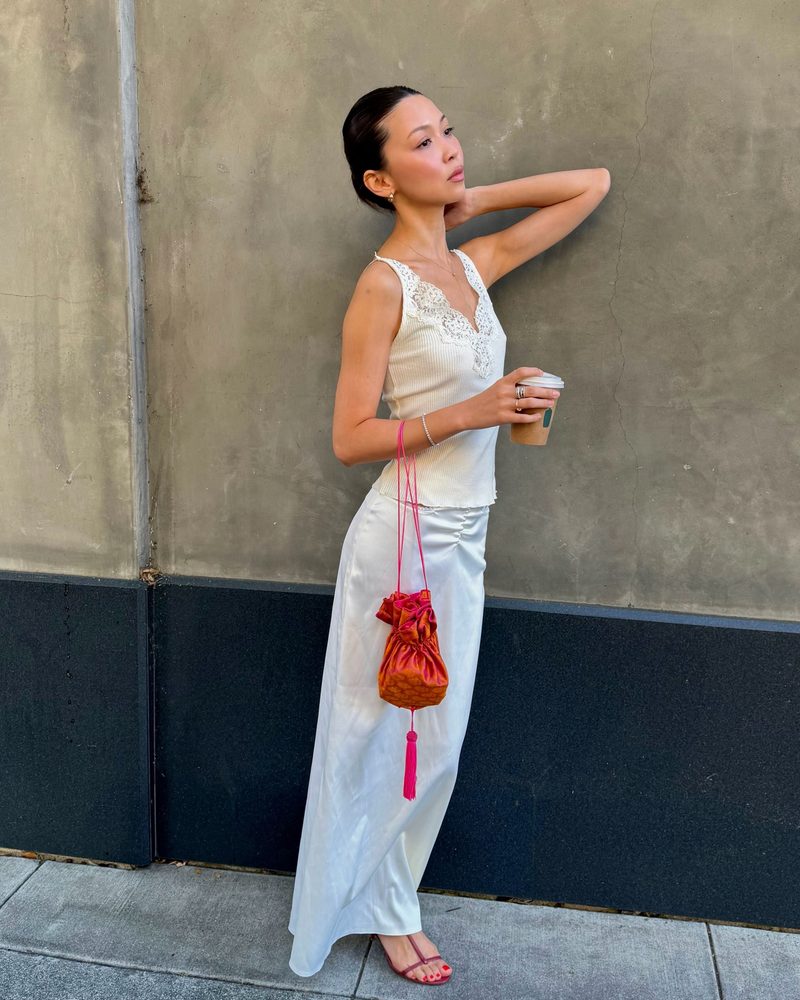 Chic look featuring an elegant white camisole paired with satin wide-leg pants%2C accessorized with a vibrant orange drawstring bag and pink sandals