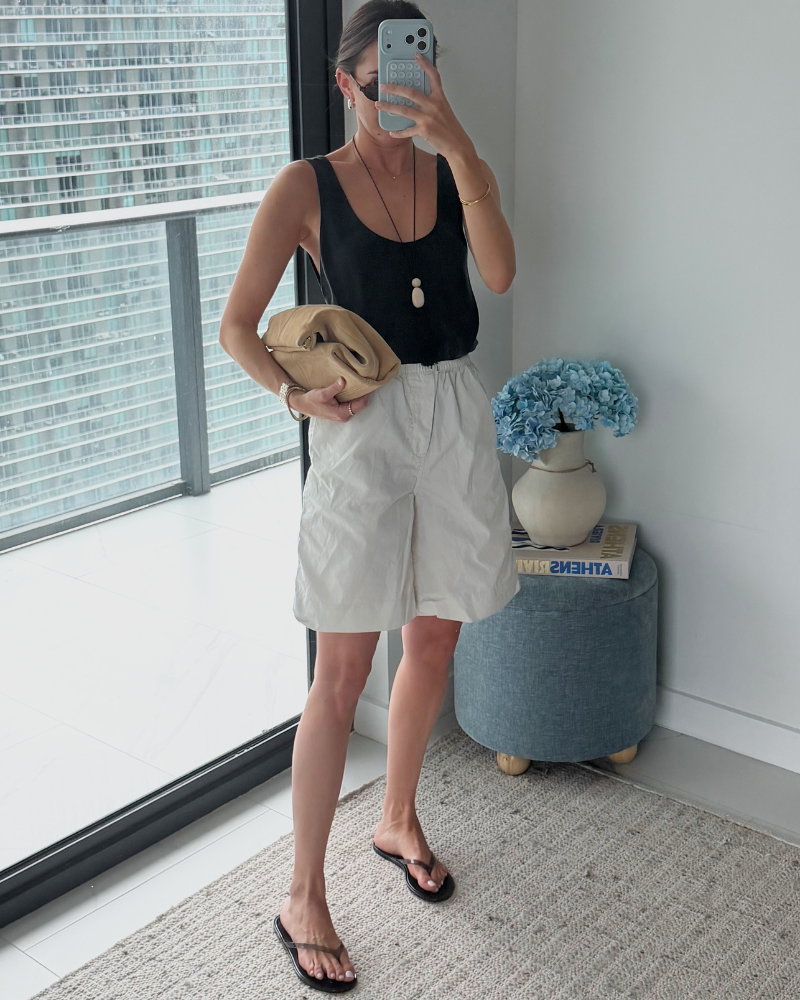 Relaxed summer outfit featuring a black scoop neck tank top paired with light beige high-waisted shorts and minimalist black flip flops.