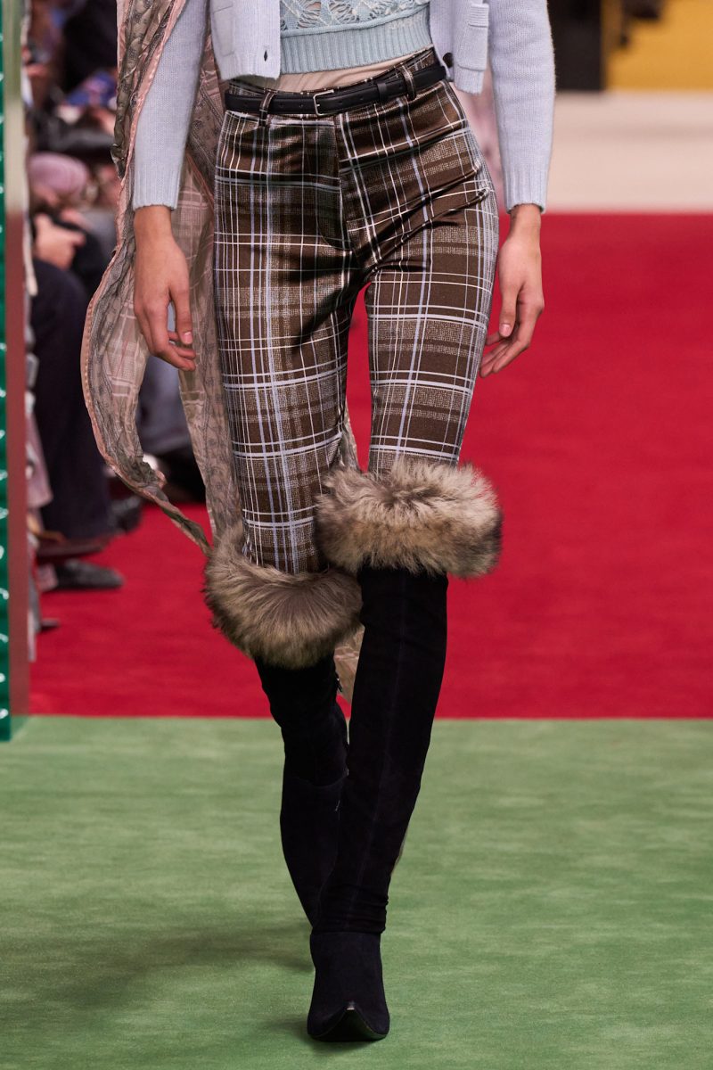 Brown plaid pants with black belt paired with black suede knee-high boots featuring fur trim at the top