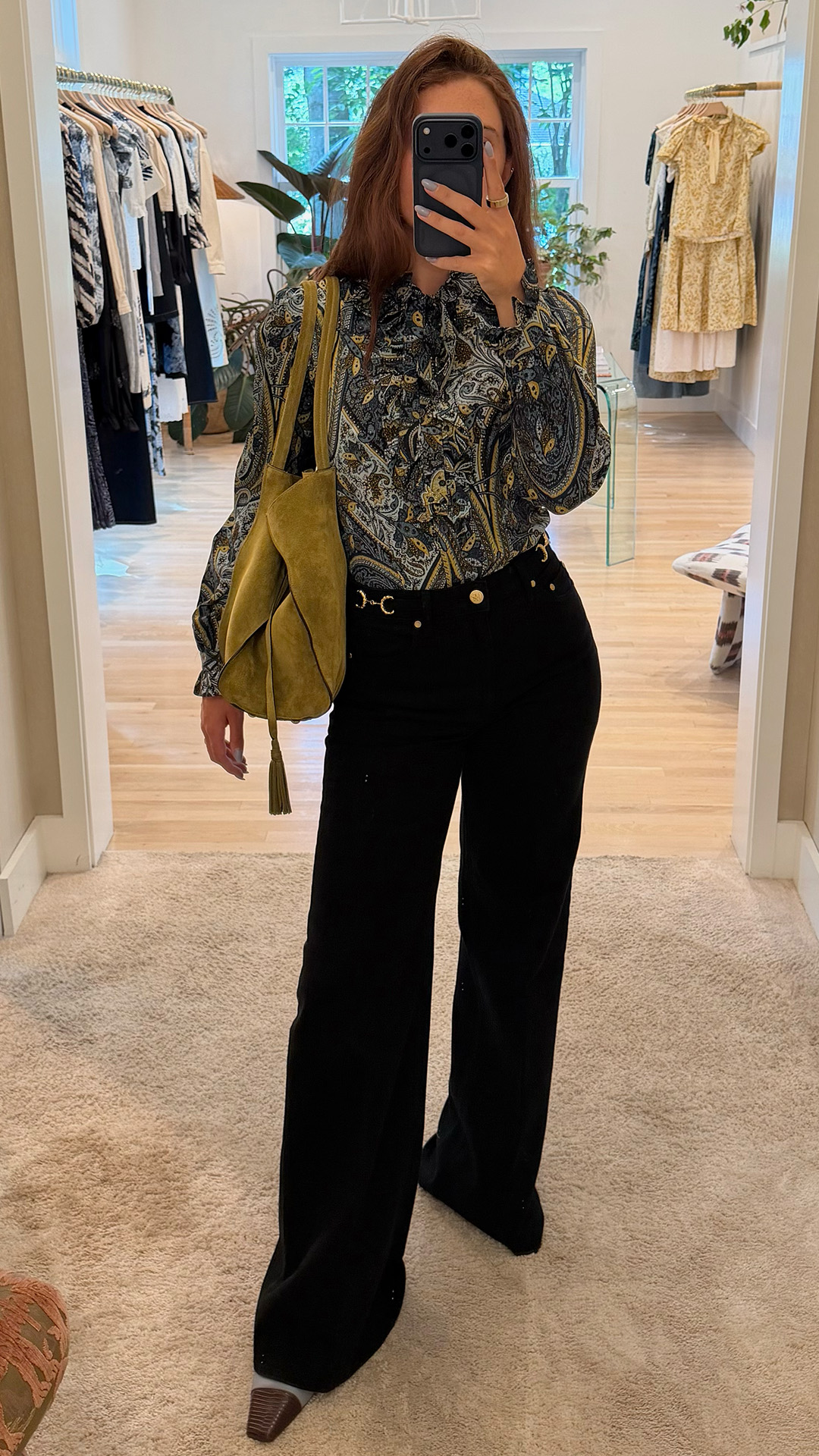 Paisley blouse styled with black wide-leg trousers and an olive suede shoulder bag in a boutique mirror selfie
